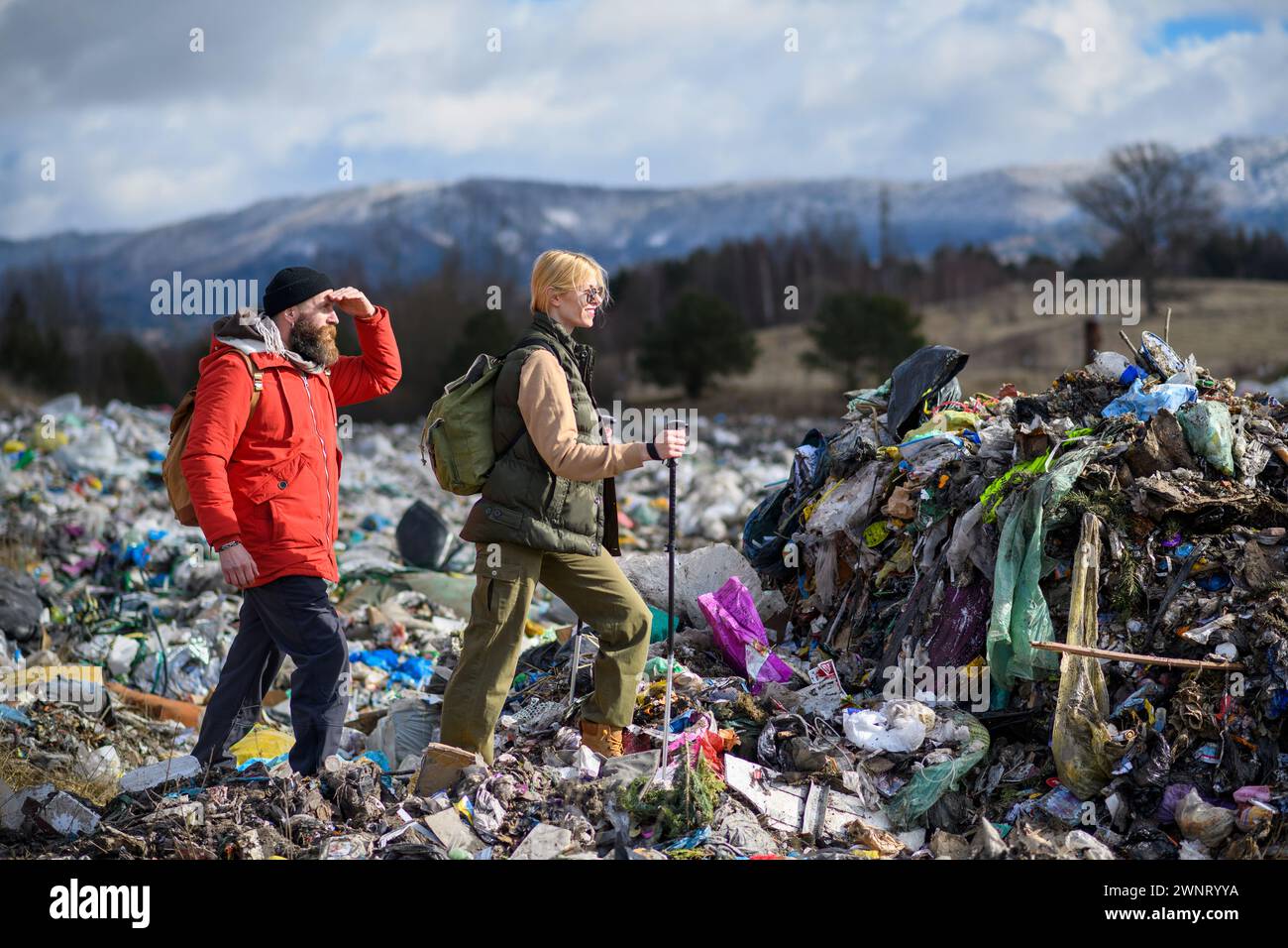 Couple of hikers walking across landfill, large pile of waste ...