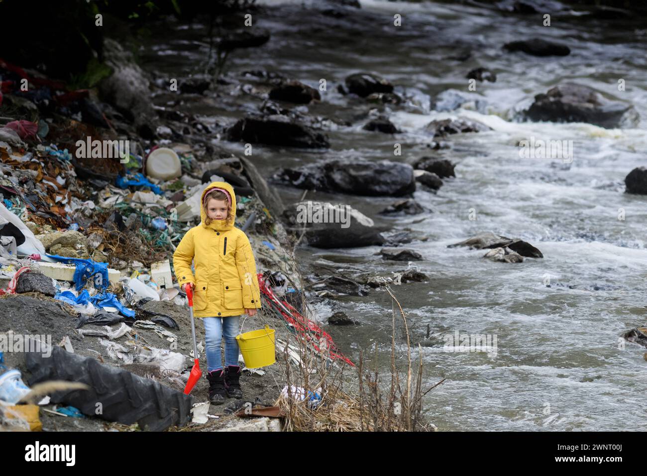 Little girl picking up litter, debris along riverbank in nature. Water ...