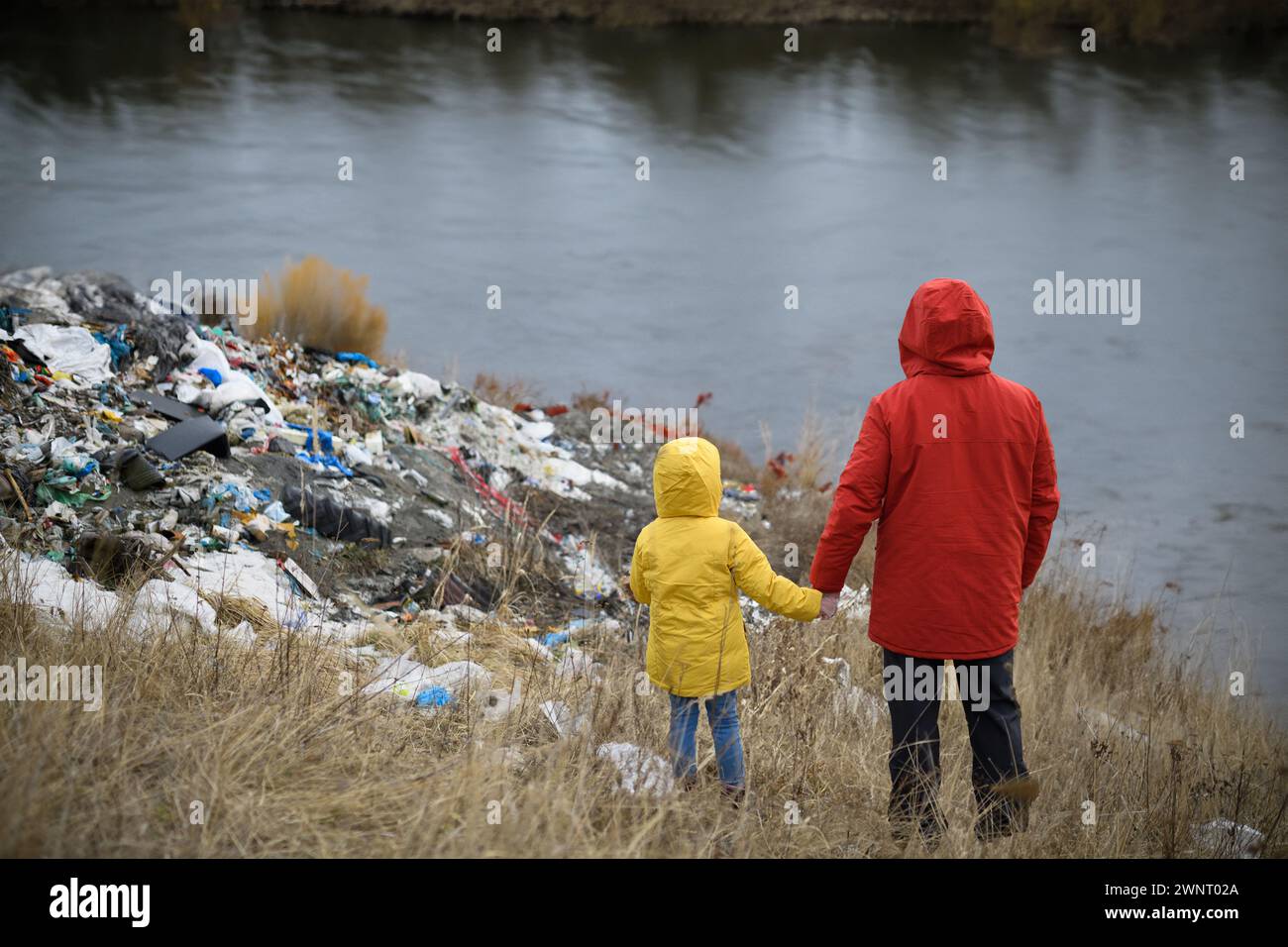 Little girl with father standing on river shore looking at piles of ...
