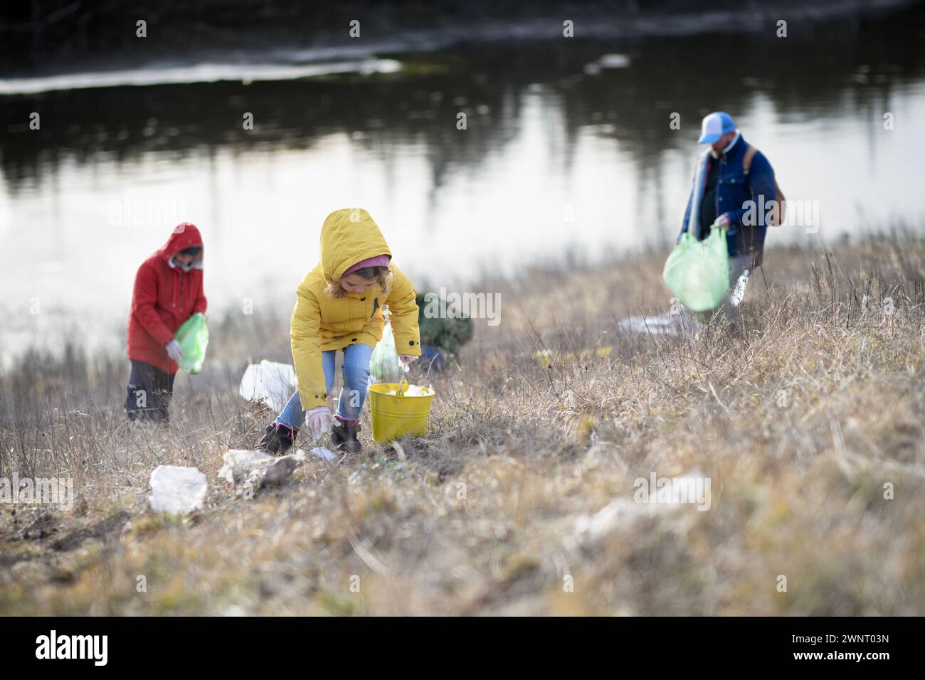 Little girl among eco activists picking up litter, along riverbank in ...