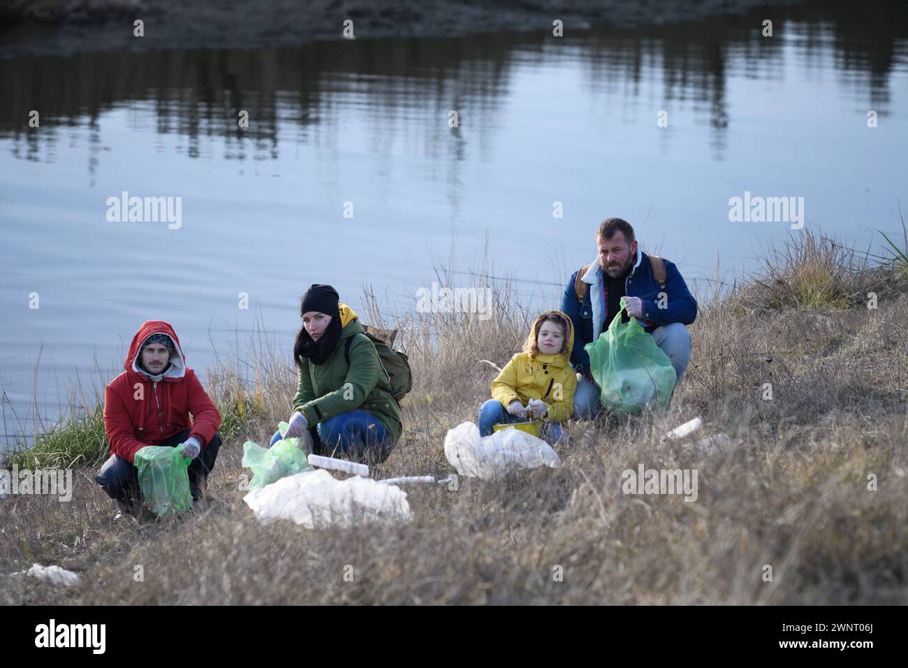 Little girl among eco activists picking up litter, along riverbank in ...