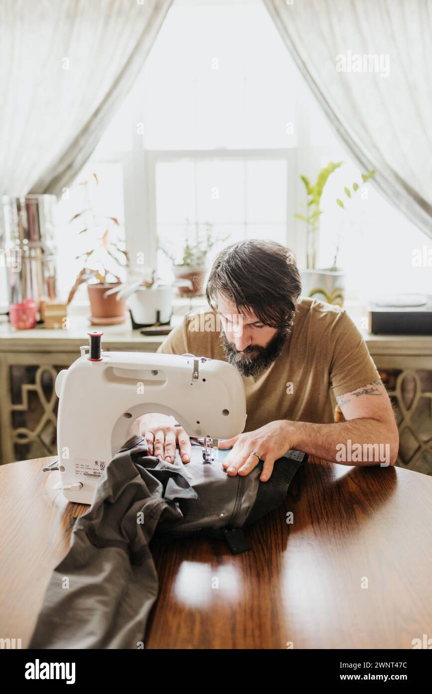 Man sits at kitchen table with sewing machine patching work pants Stock ...