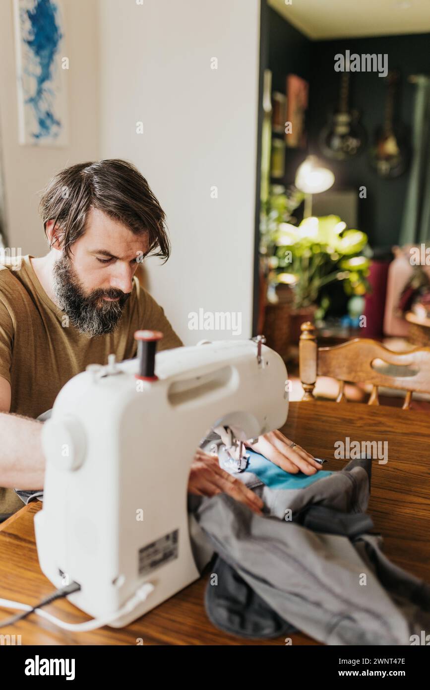 Man sits at kitchen table with sewing machine patching work pants Stock ...