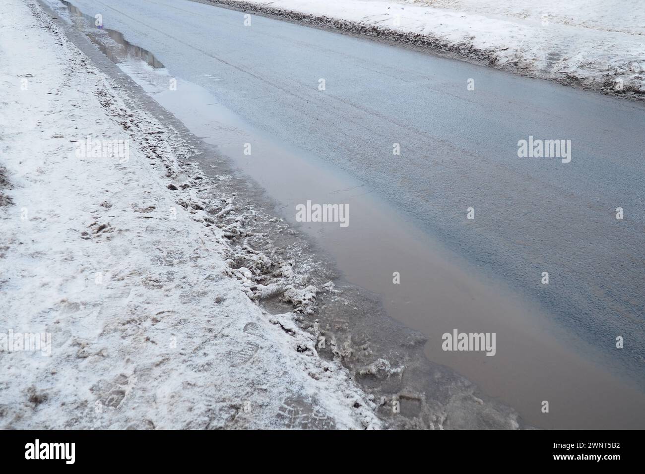 Ice on city roads. Wet asphalt with sand. Snow-covered roadsides ...