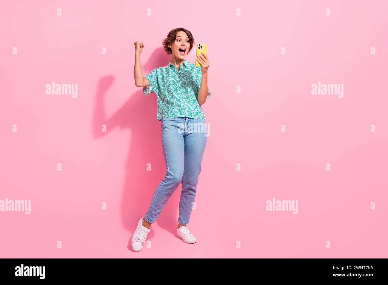 Full length photo of glad overjoyed person raise fist use smart phone ...
