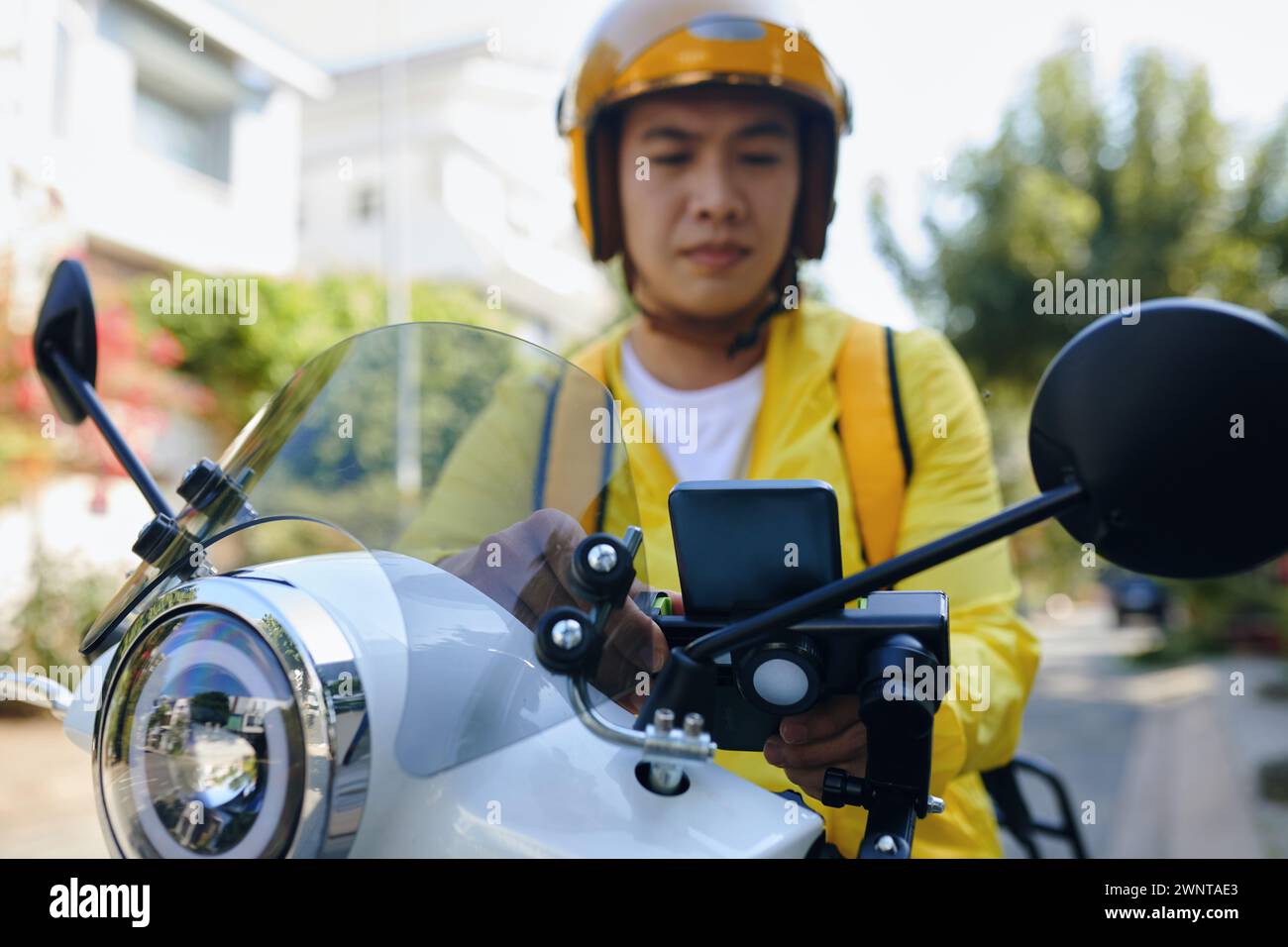 Man working as taxi driver sitting on motorbike and setting mobile app ...