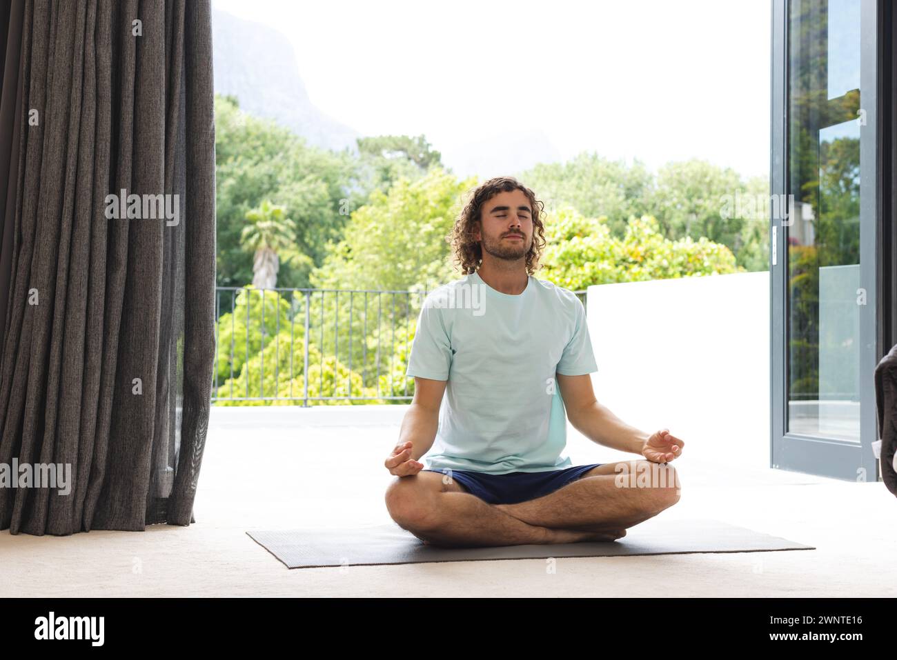 Young Caucasian man meditates in a serene indoor setting, eyes closed ...
