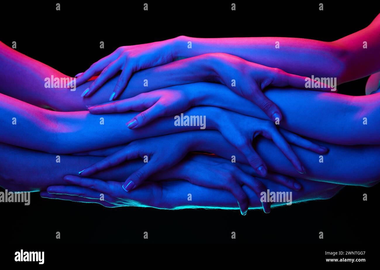 Overlapping hands in multicolored neon lighting against black studio ...