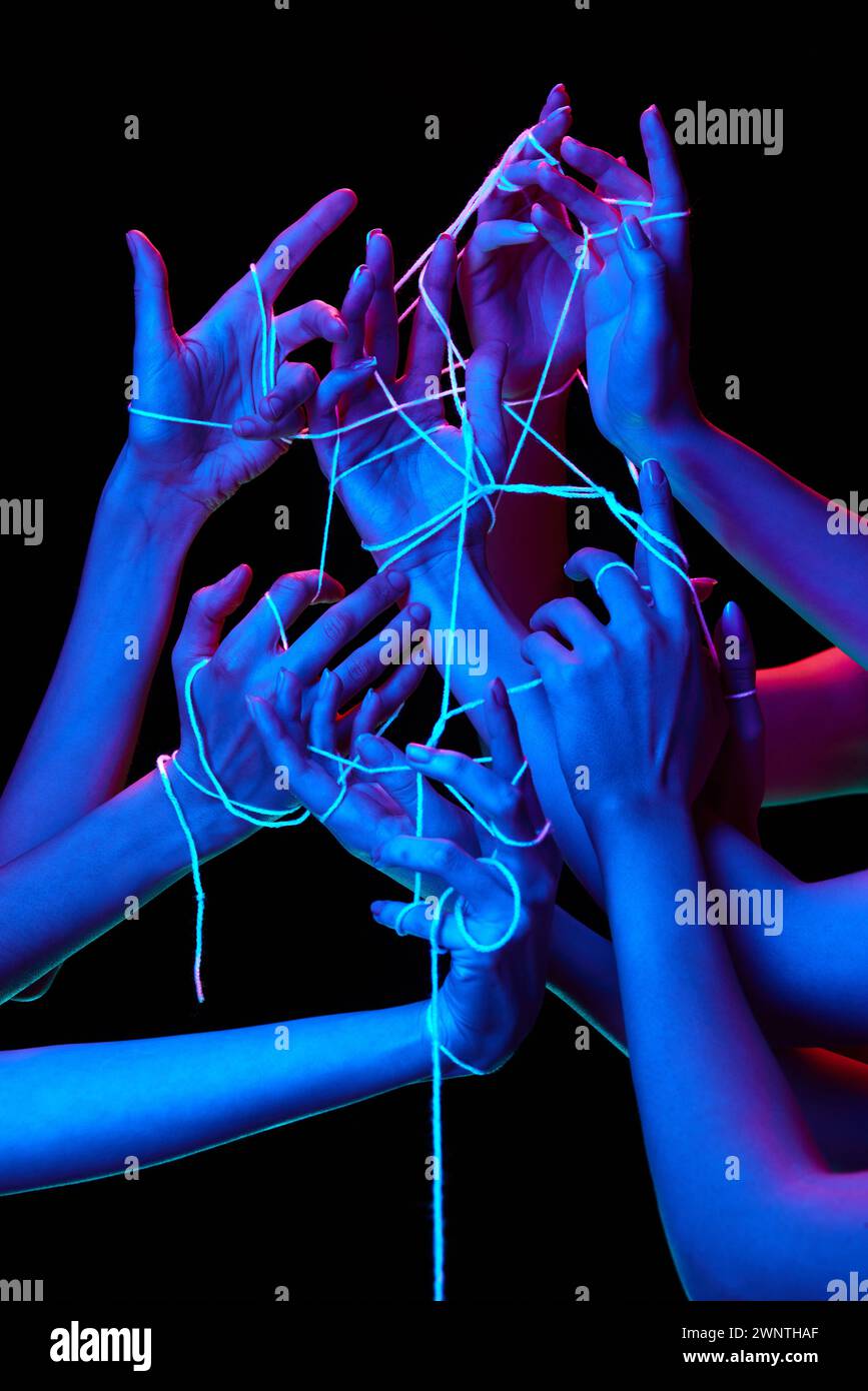 Strings entangled by multiple hands in multicolored neon lighting against black studio ...