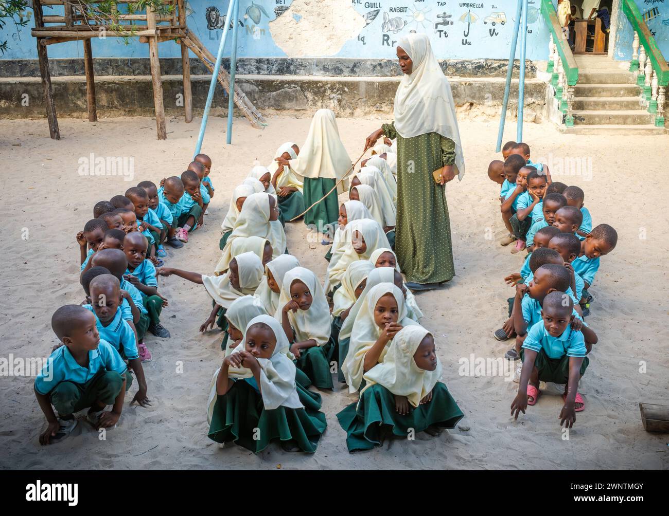 A teacher with a stick supervises young muslim boys and girls at ...