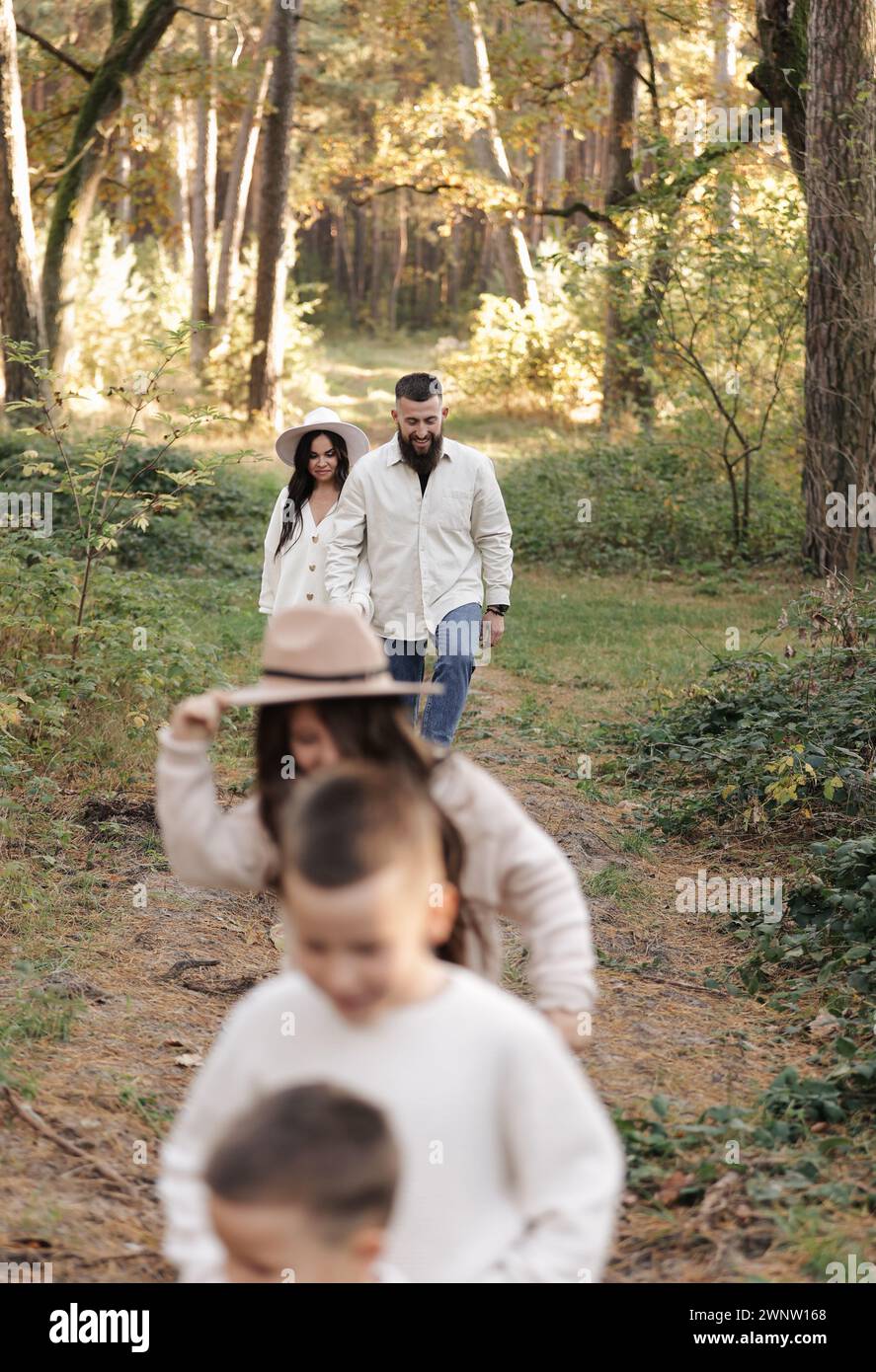 Young mother, father with daughter and sons are walking, having fun in autumn forest. Family ...