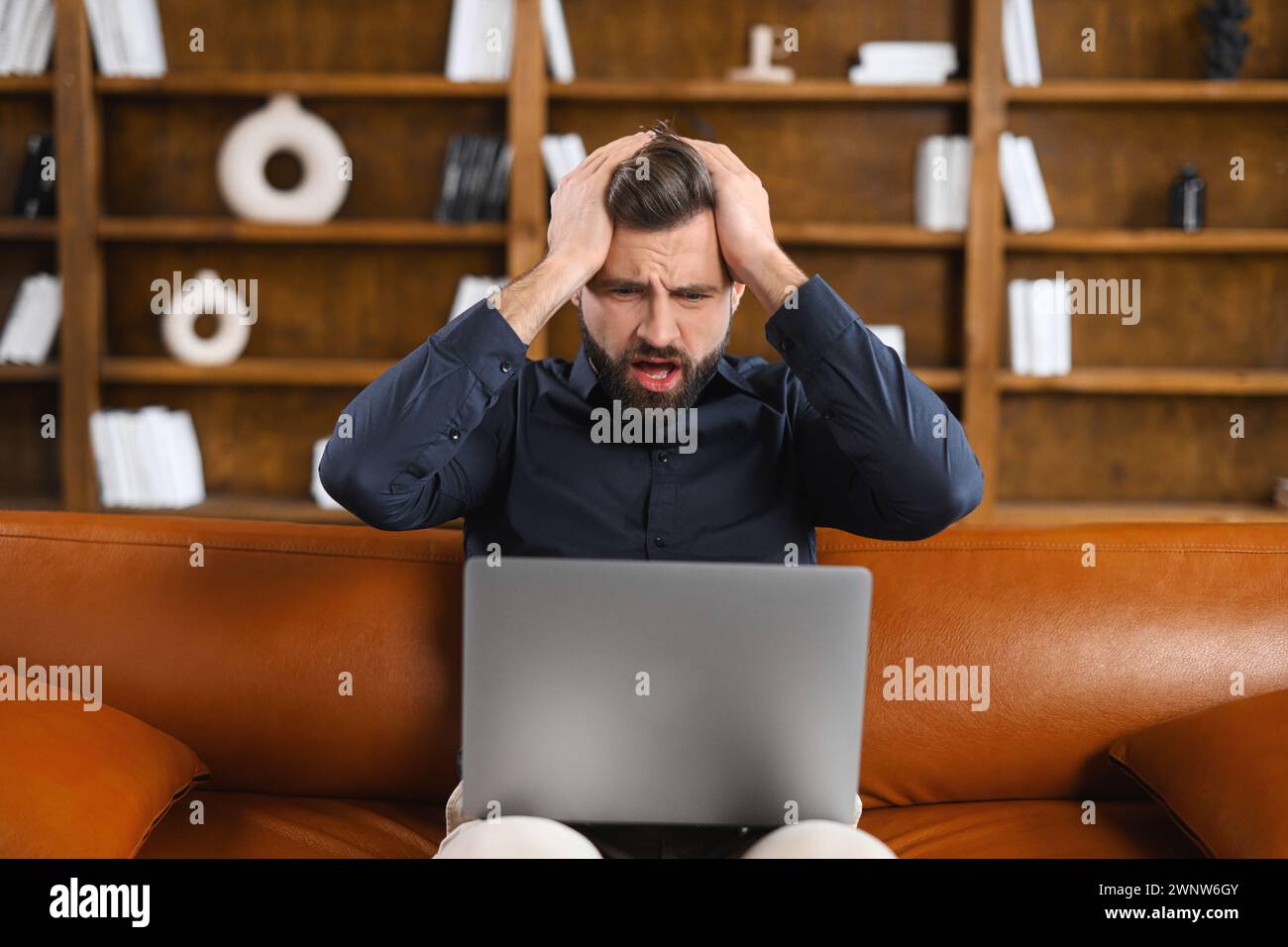 An unhappy young male freelancer looks at a laptop screen shocked by ...