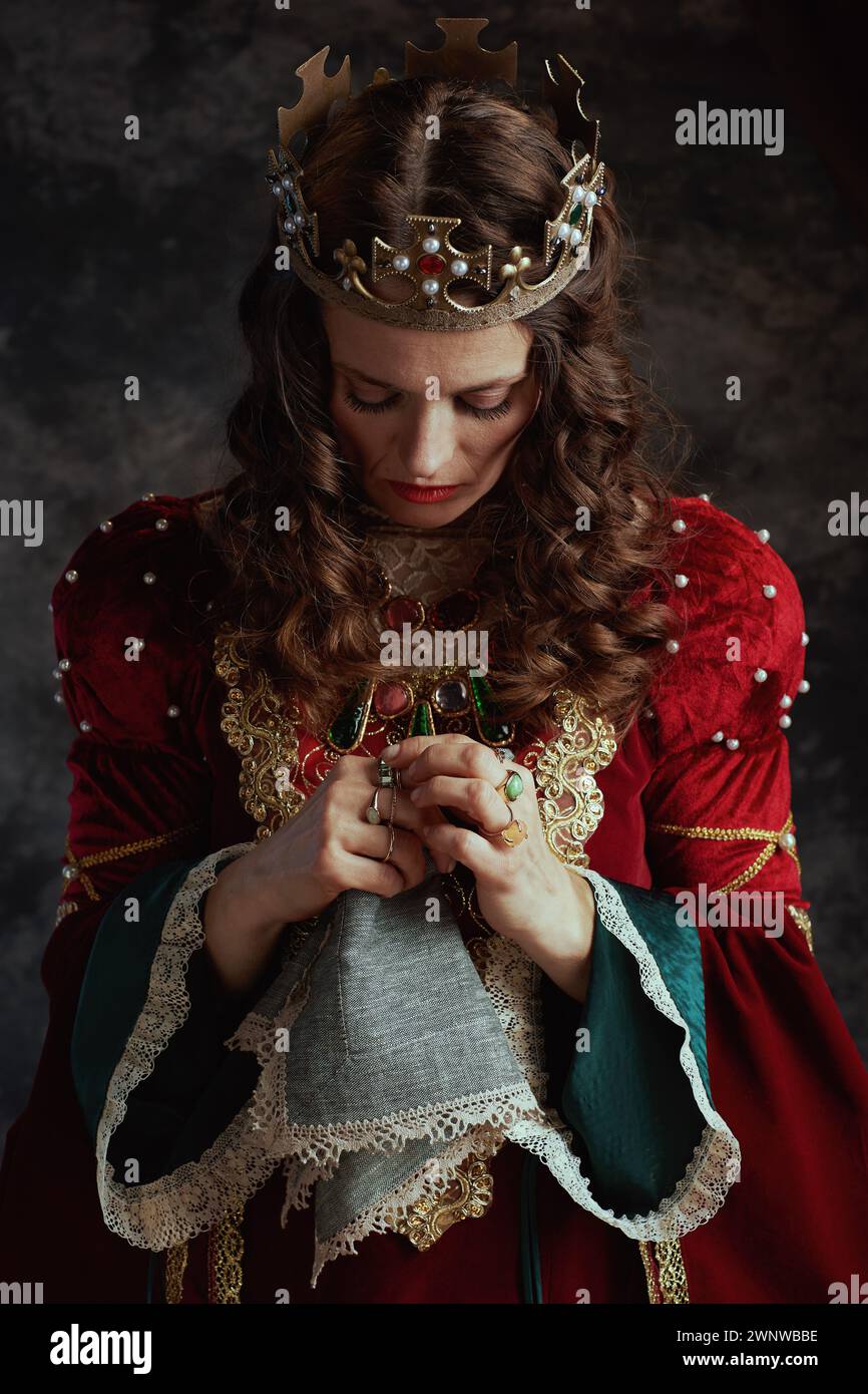 sad medieval queen in red dress with handkerchief and crown on dark ...
