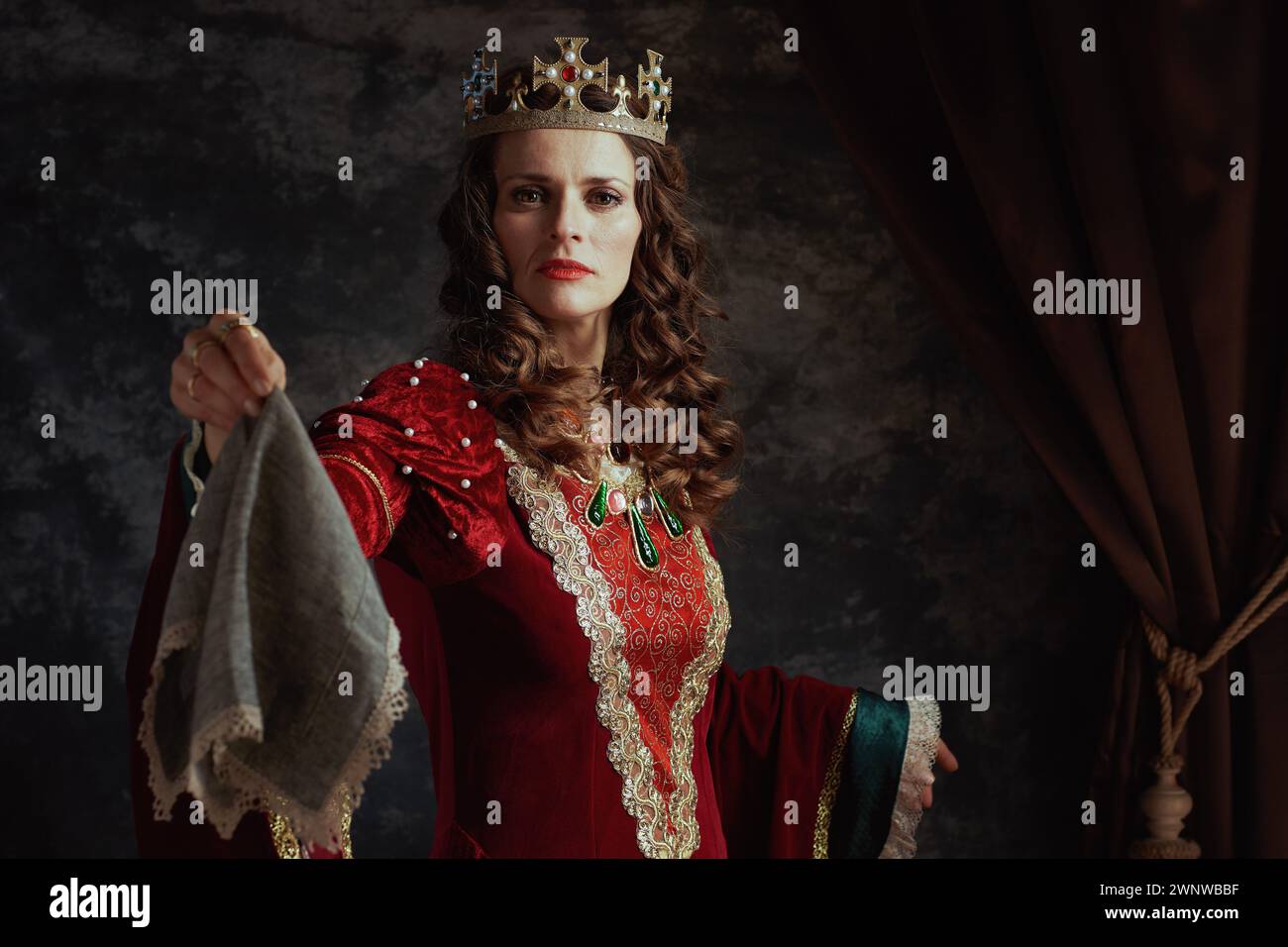medieval queen in red dress with handkerchief and crown on dark gray ...