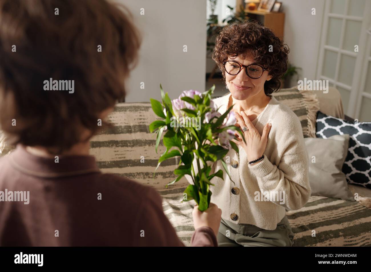 Young surprised woman in eyeglasses looking at bunch of flowers being ...