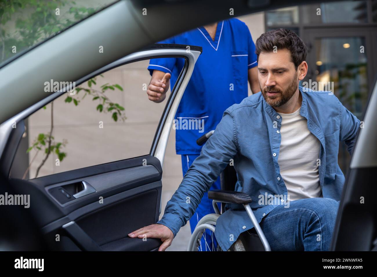 Disabled man getting on a car, male nurse helping him Stock Photo - Alamy