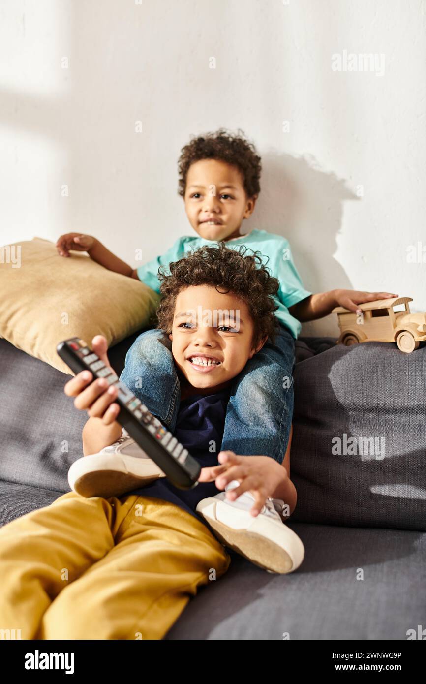 merry african american cute boys holding remote control and wooden toy car and watching movies ...