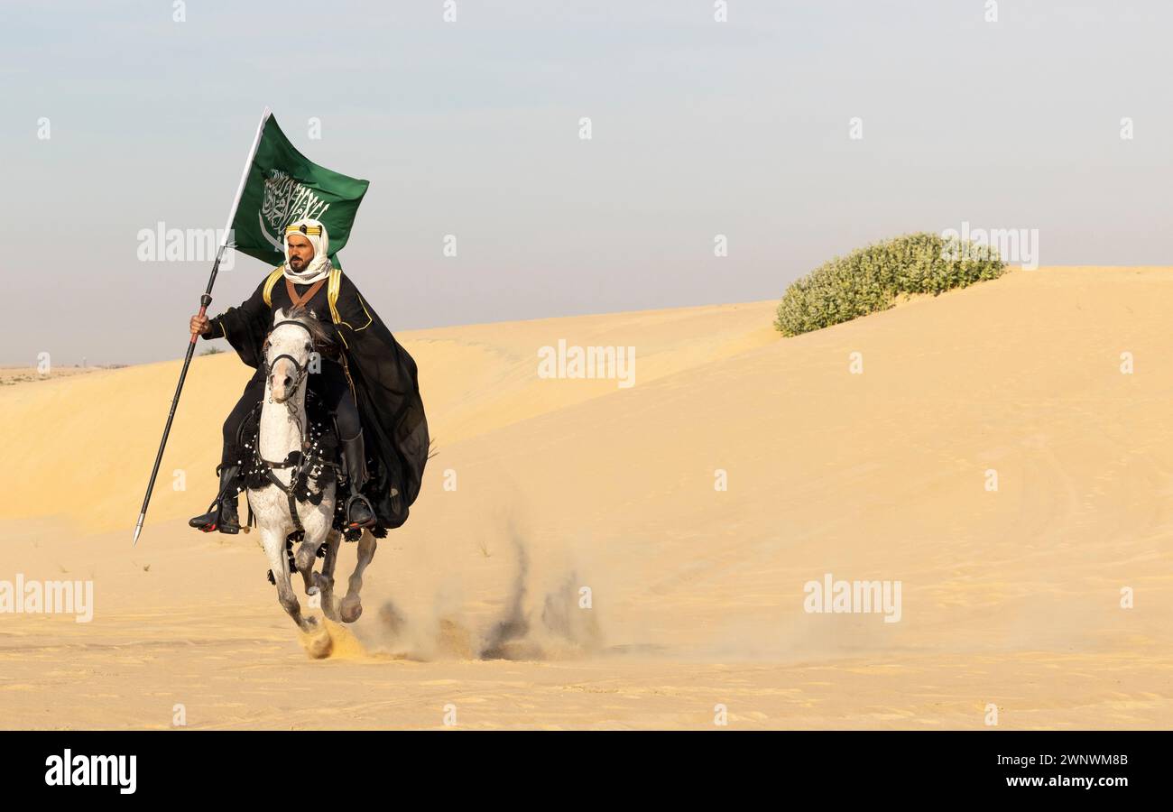 Man in traditional clothing with his horse in a desert, carrying a flag ...