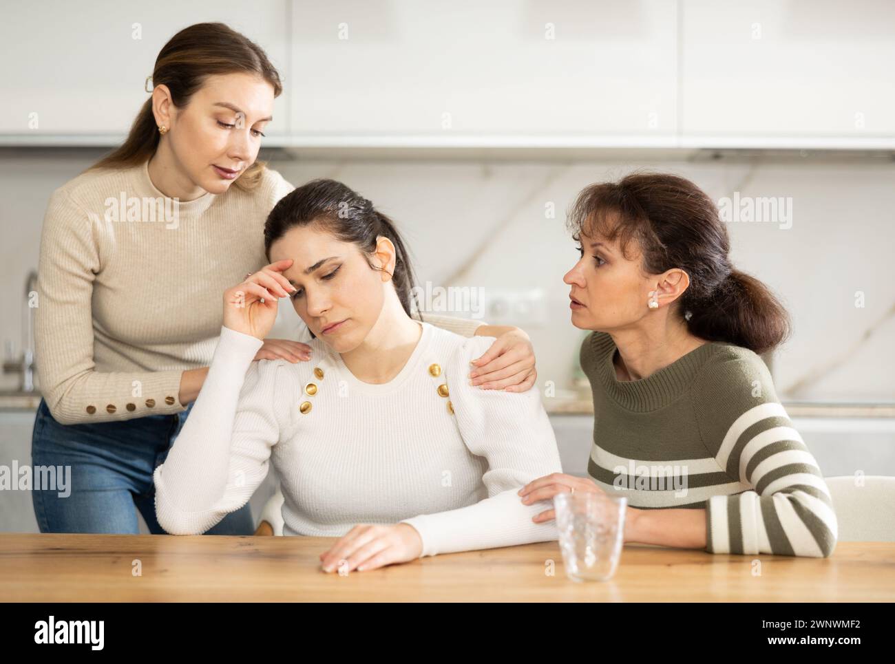 Sad middle-aged woman sitting at table while two others trying to calm ...