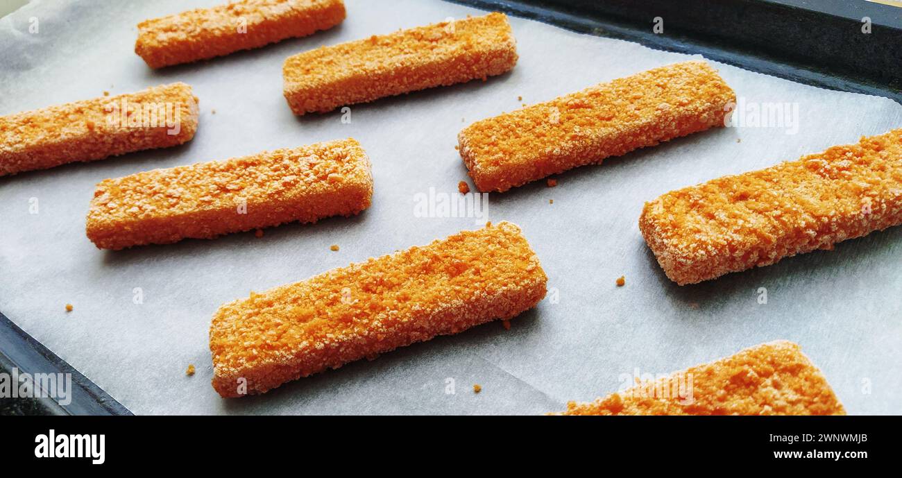 Frozen fish sticks are laid out on baking paper. Cooking a fish ...