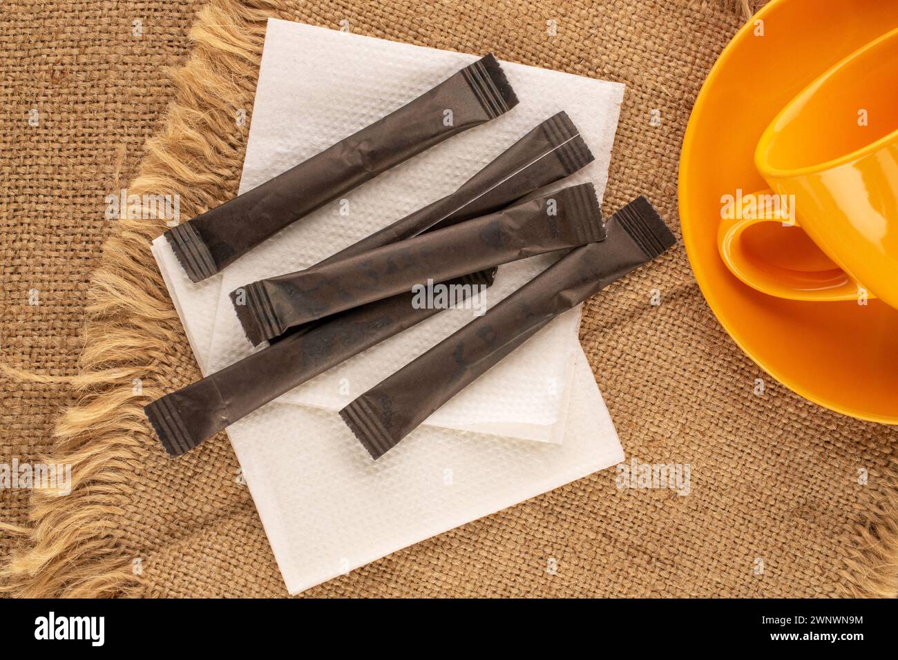 Several paper sugar sticks with ceramic cup and saucer on jute cloth ...