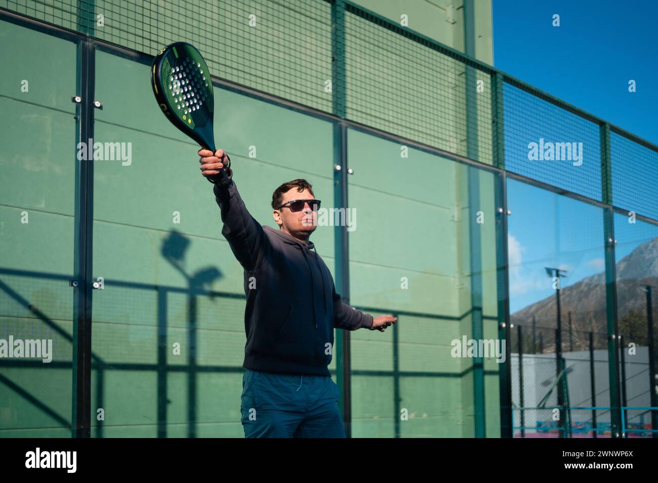 A man prepares for a backhand shot in padel tennis, with a focused ...