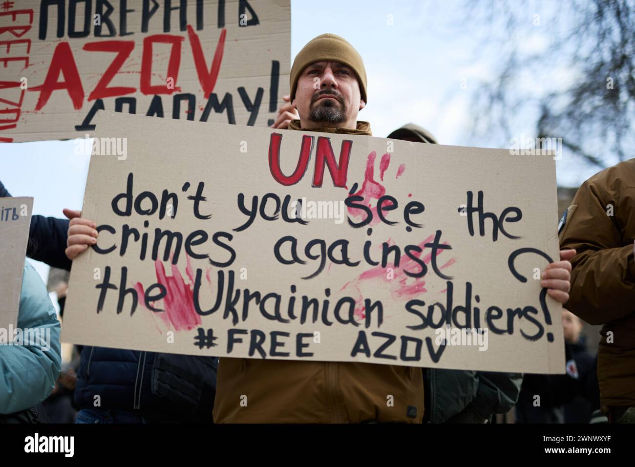 Ukrainian military person holds a banner: "UN. Don't You See The Crimes ...