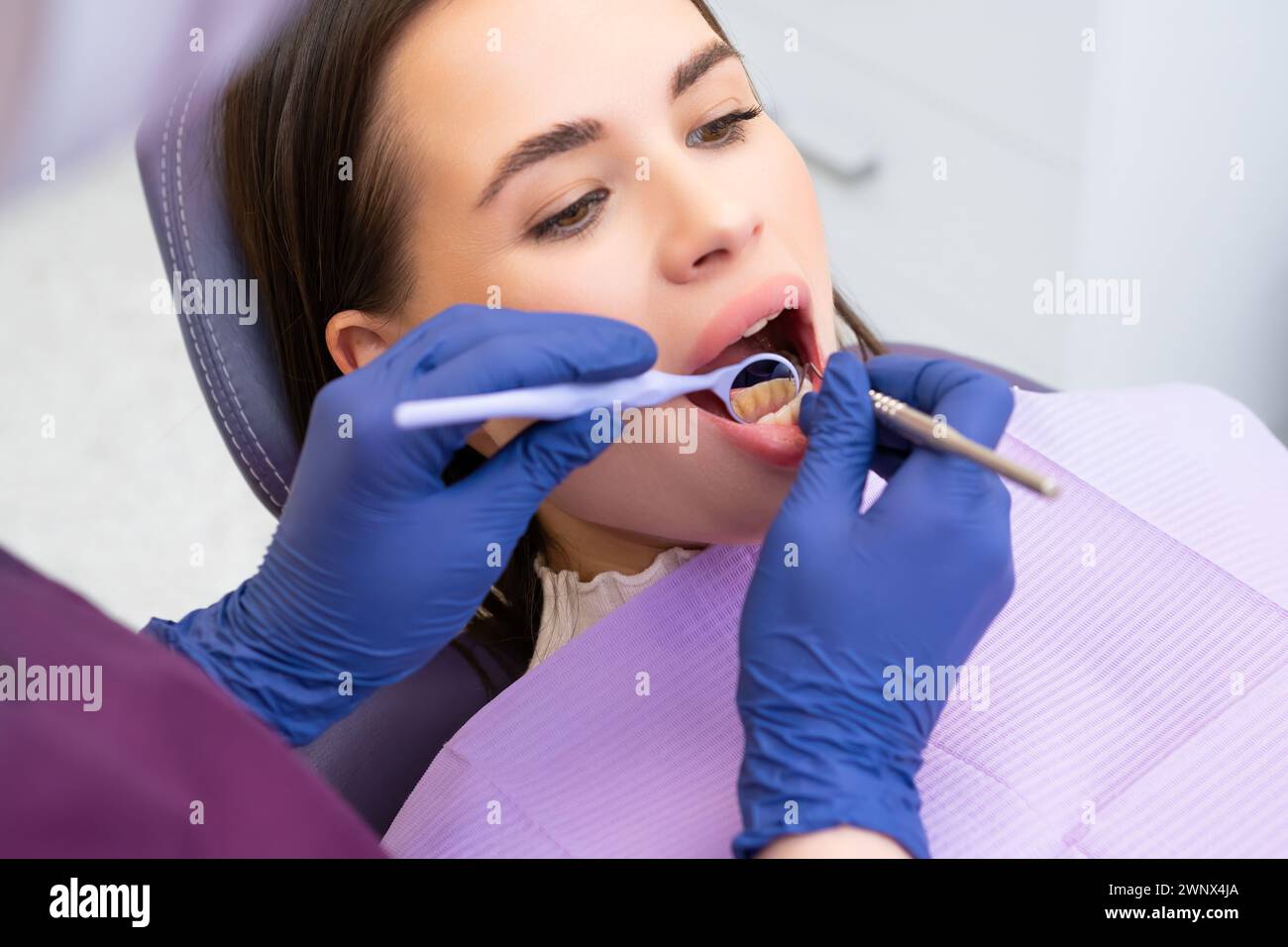 Over the shoulder view of a dentist examining a female patients teeth ...