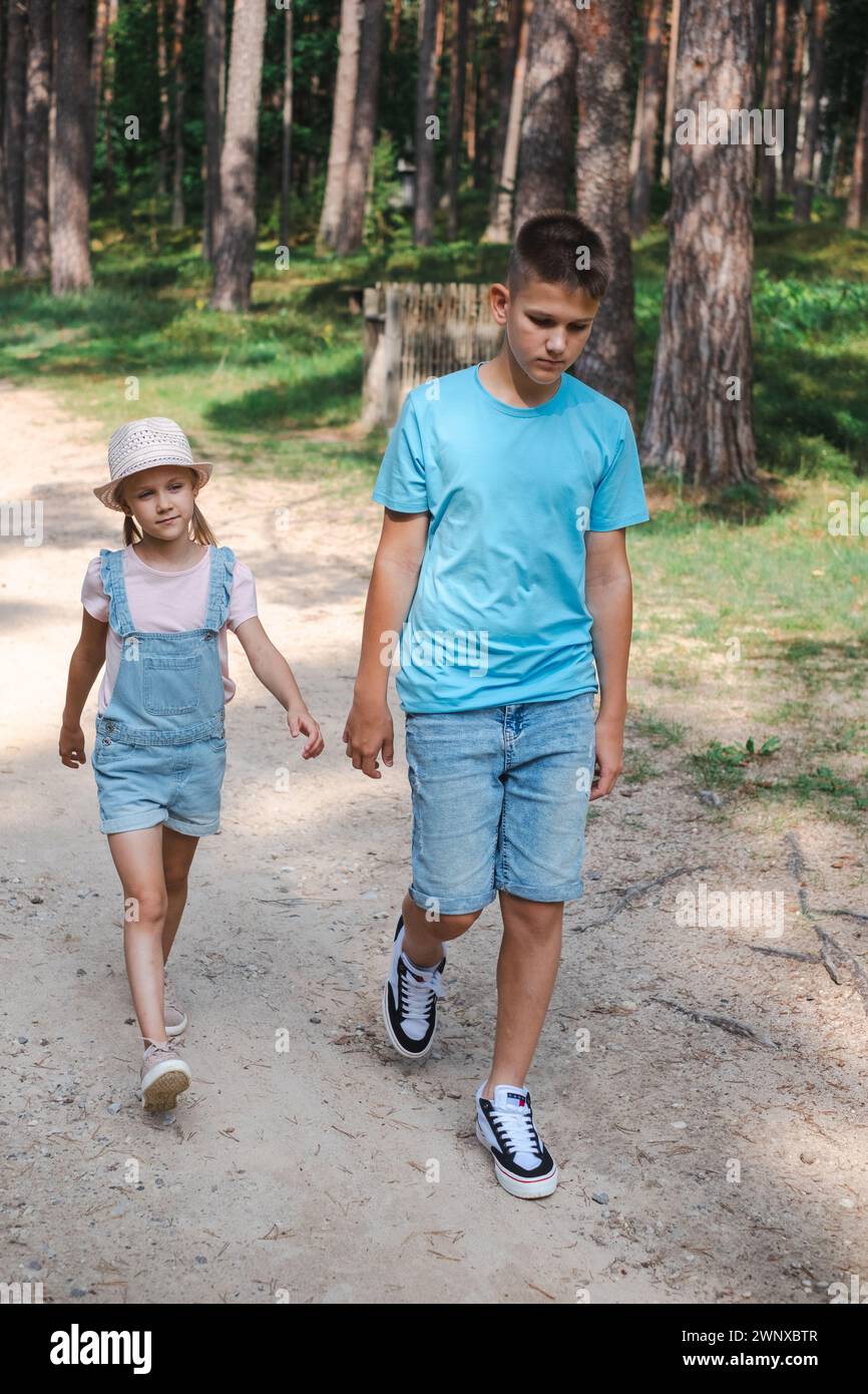 A teenage boy in a blue T-shirt walking with a young girl in denim ...