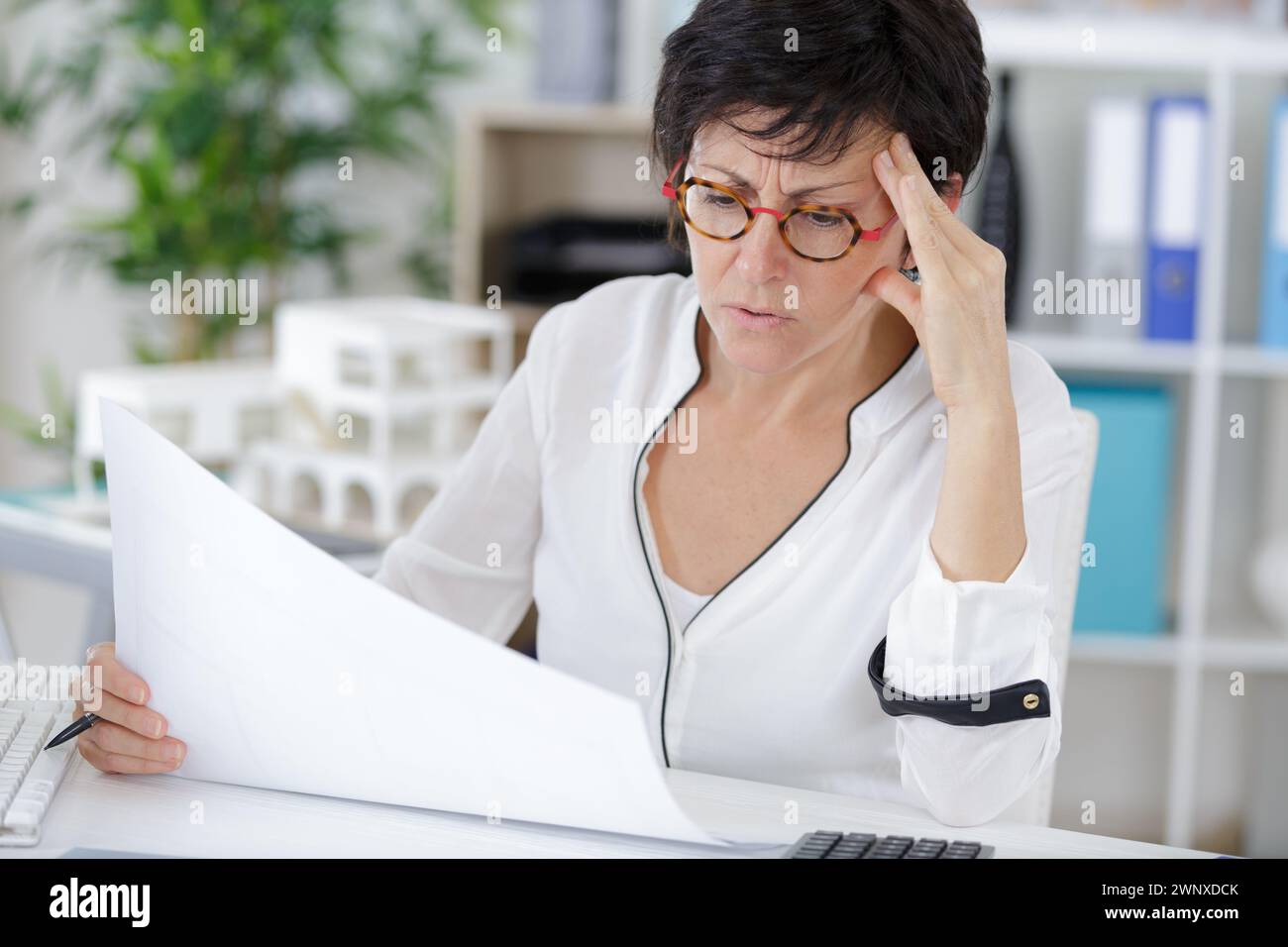 stressed upset female engineer wearing spectacles looking at blueprints ...