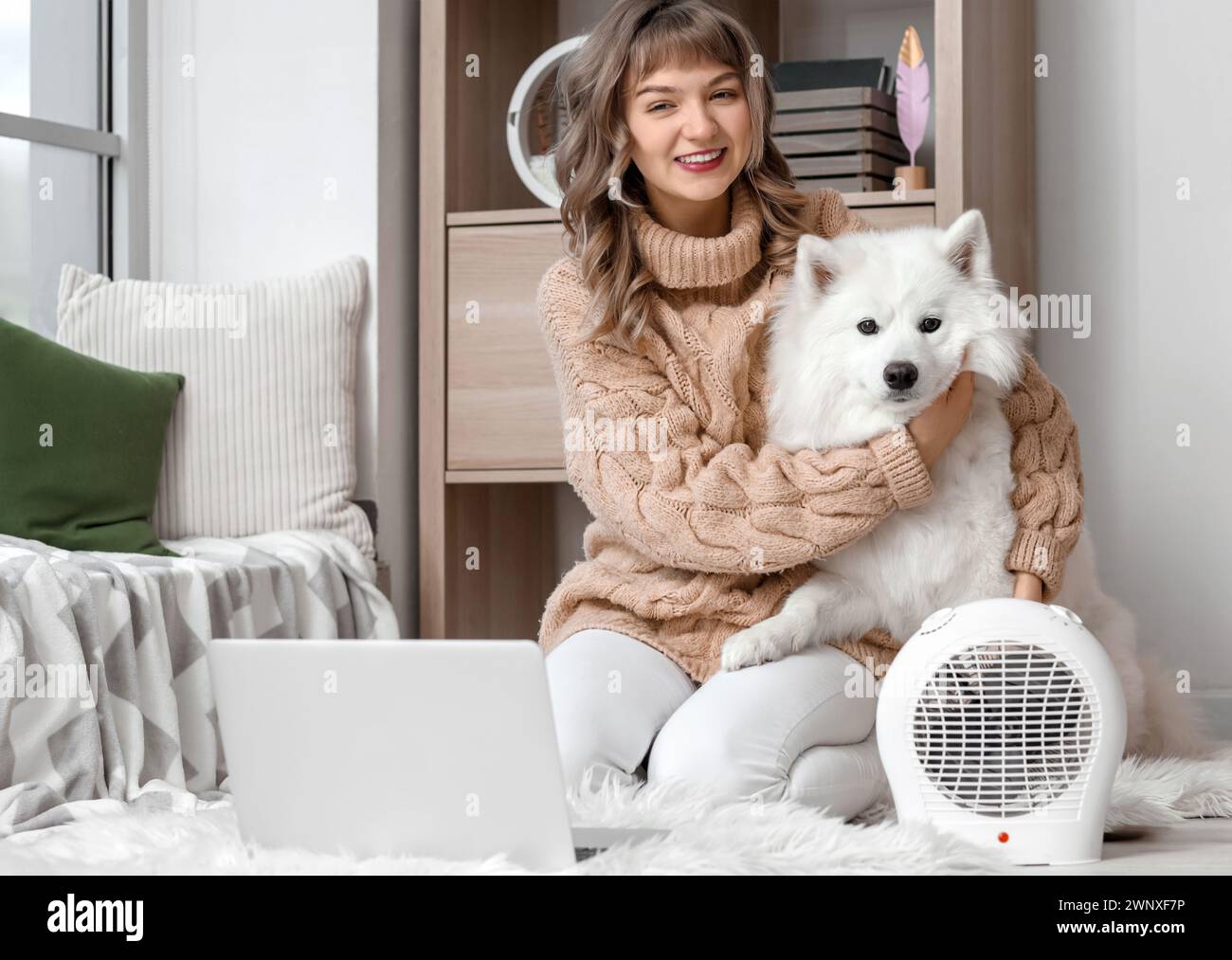 Young woman with Samoyed dog and laptop warming near electric fan ...