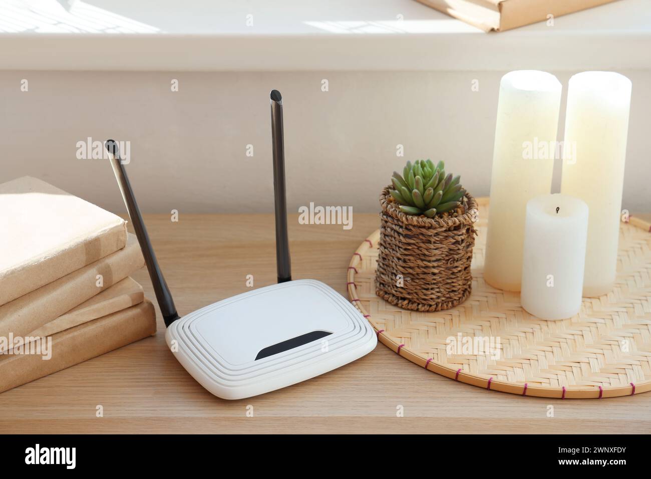 Modern wi-fi router with books, plant and candles on shelf in room ...