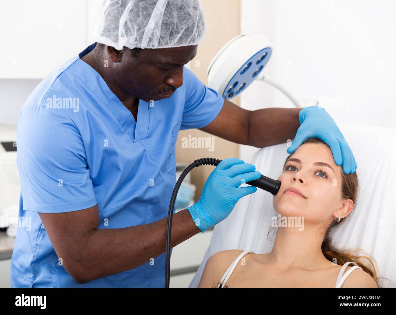 Experienced beautician performing female face skin rf lifting procedure ...