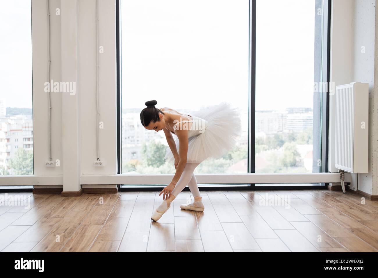 Ballerina stretching to feet while standing in dance studio with large ...