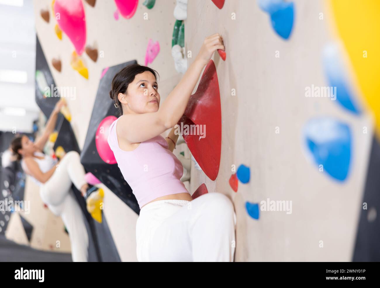 Asian girl is focused on climbing to top of artificial bouldering wall ...