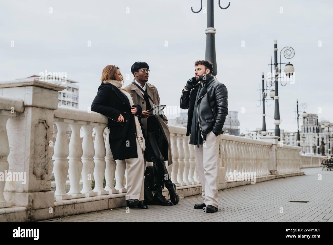 Three friends engage in a lively conversation on a city bridge, against ...