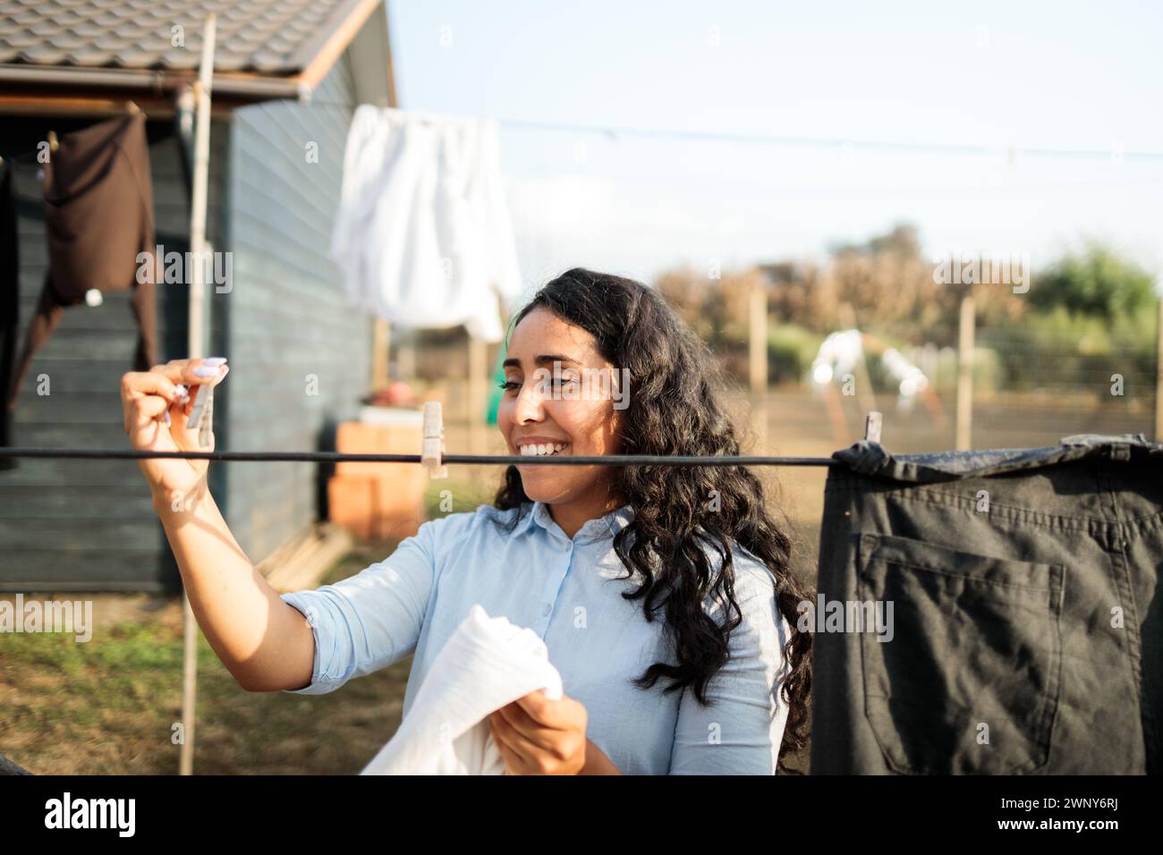 Latin young woman hanging clothes to dry in the yard of her house in ...