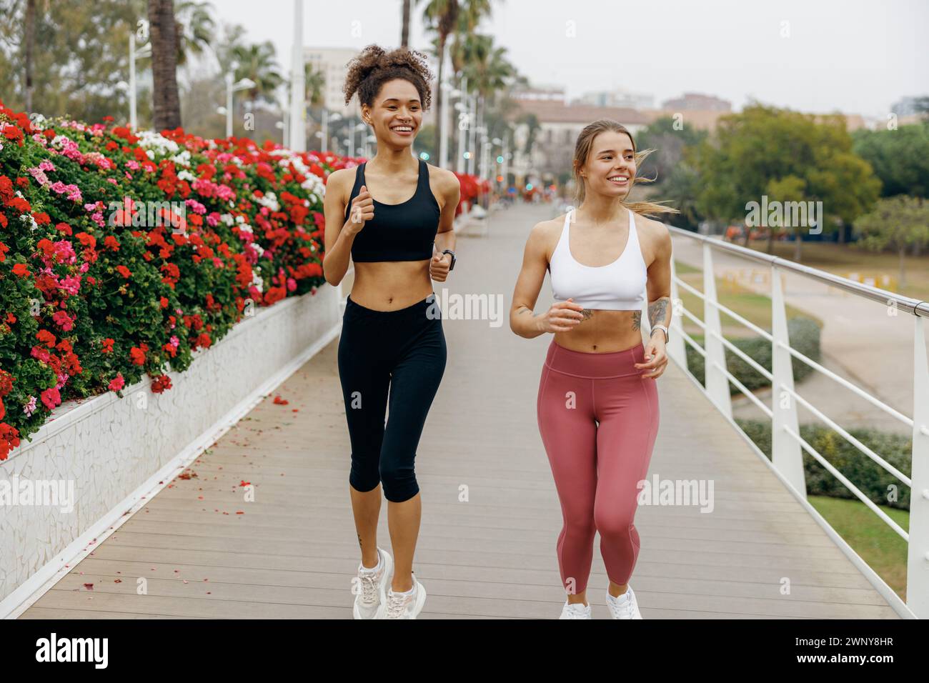 Two smiling women athlete running side by side along an outdoor track ...