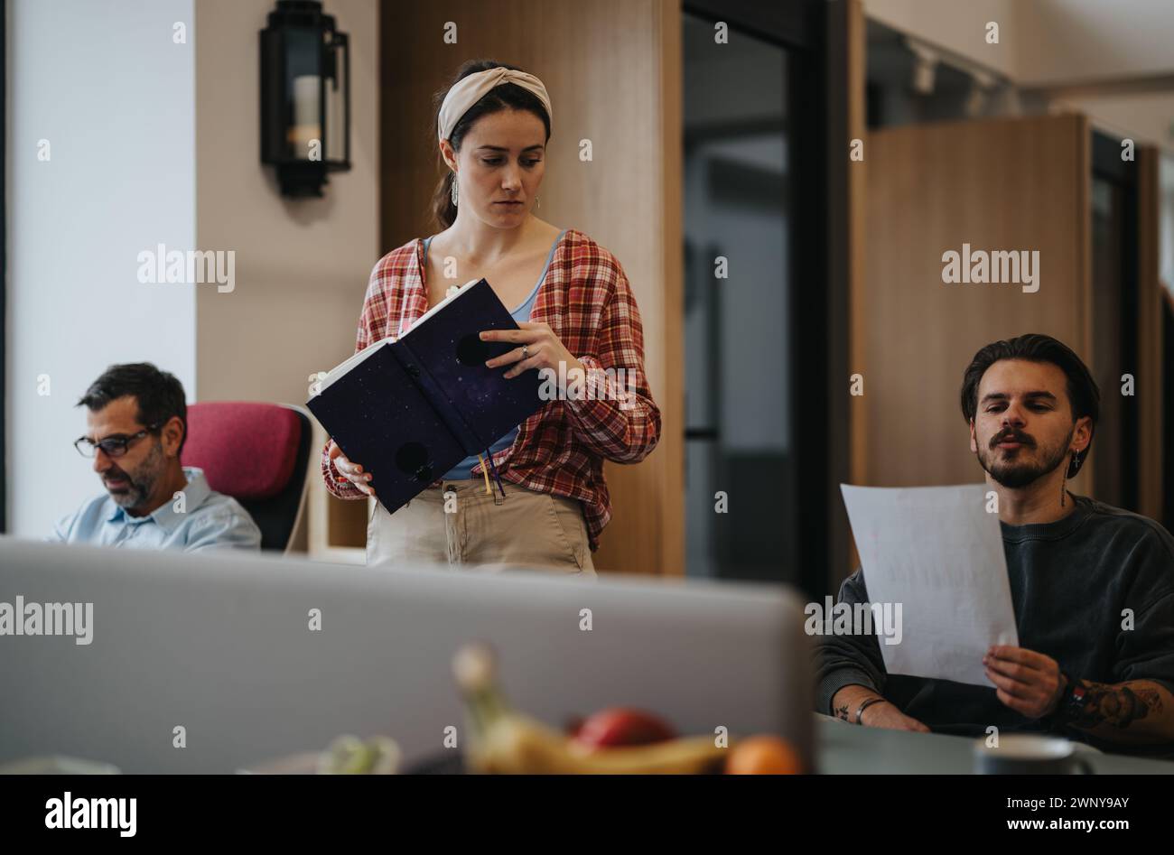 A dedicated female employee reviews a binder while male colleagues work ...