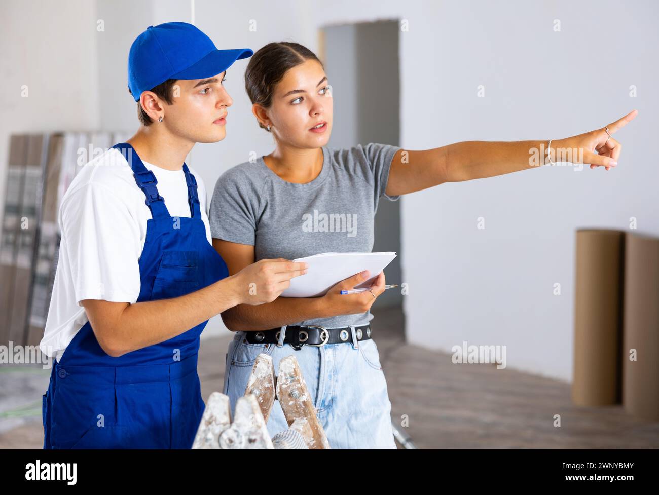 Girl homeowner discussing house renovation work plan with young builder ...