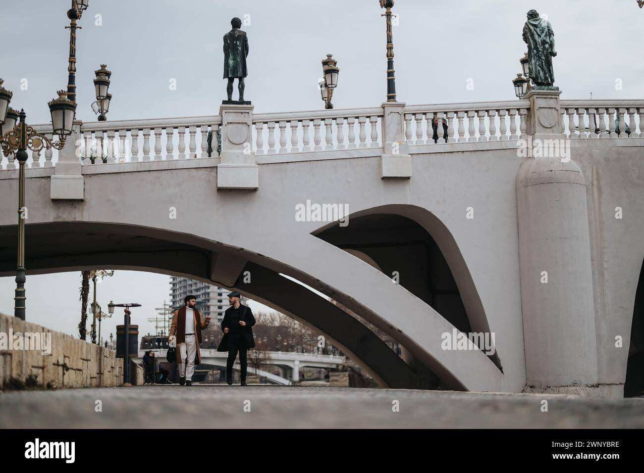 This image captures two fashionable men engaged in a conversation while ...