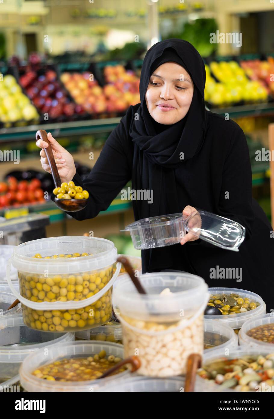 Asian woman in dark blue hijab puts handful of olives in disposable ...