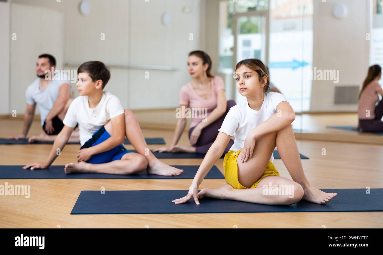 Tween girl doing twisting asana Matsyendrasana during family yoga class ...
