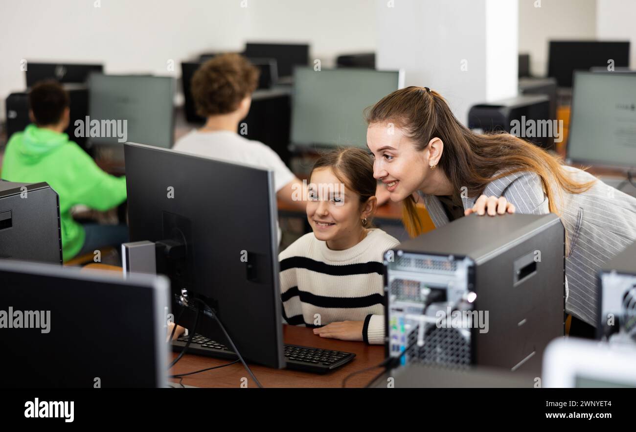 Smiling female teacher talking to happy teenage girl in computer class ...