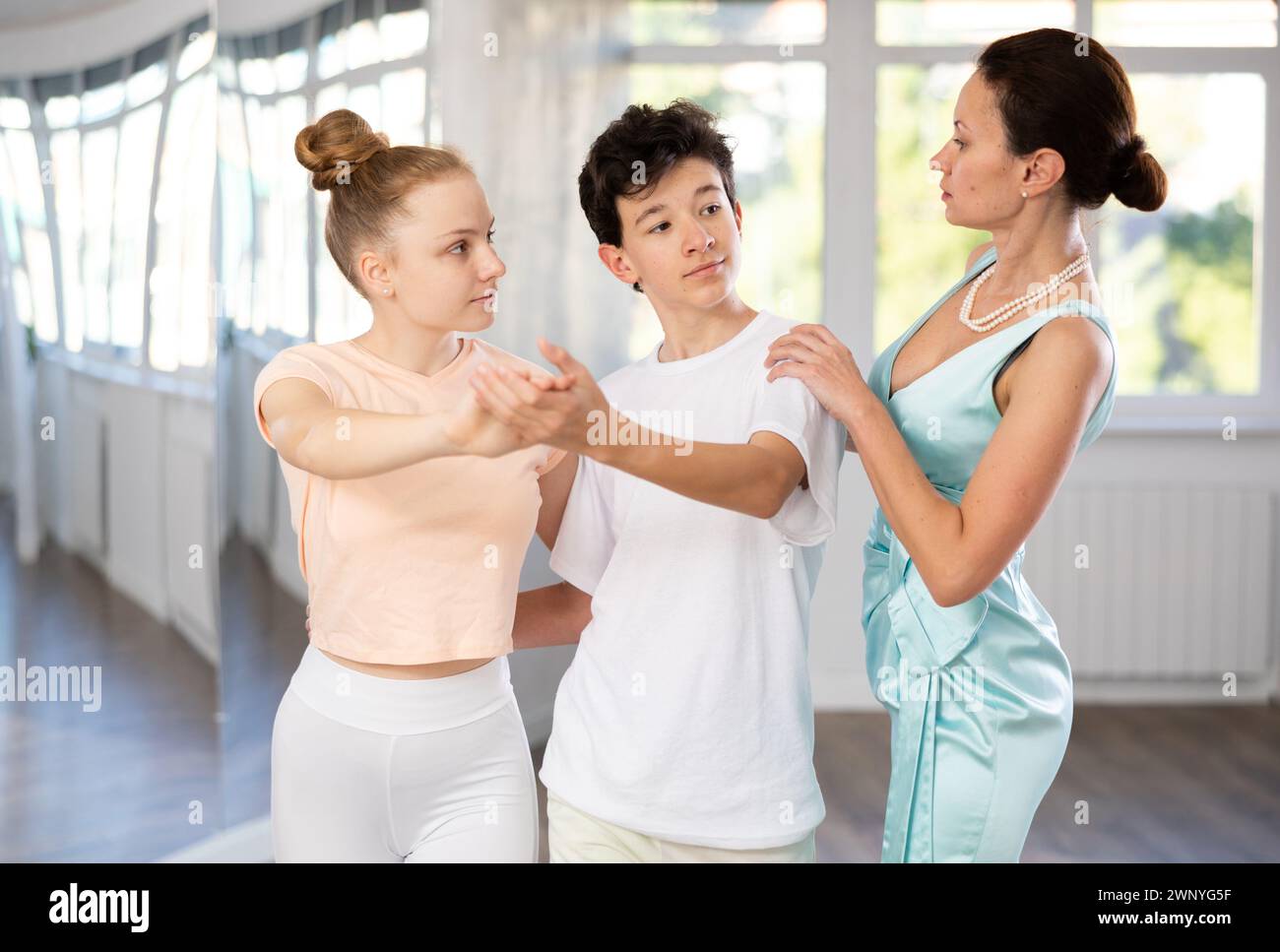 Teenage couple practicing ballroom dance with female teacher adjusting ...
