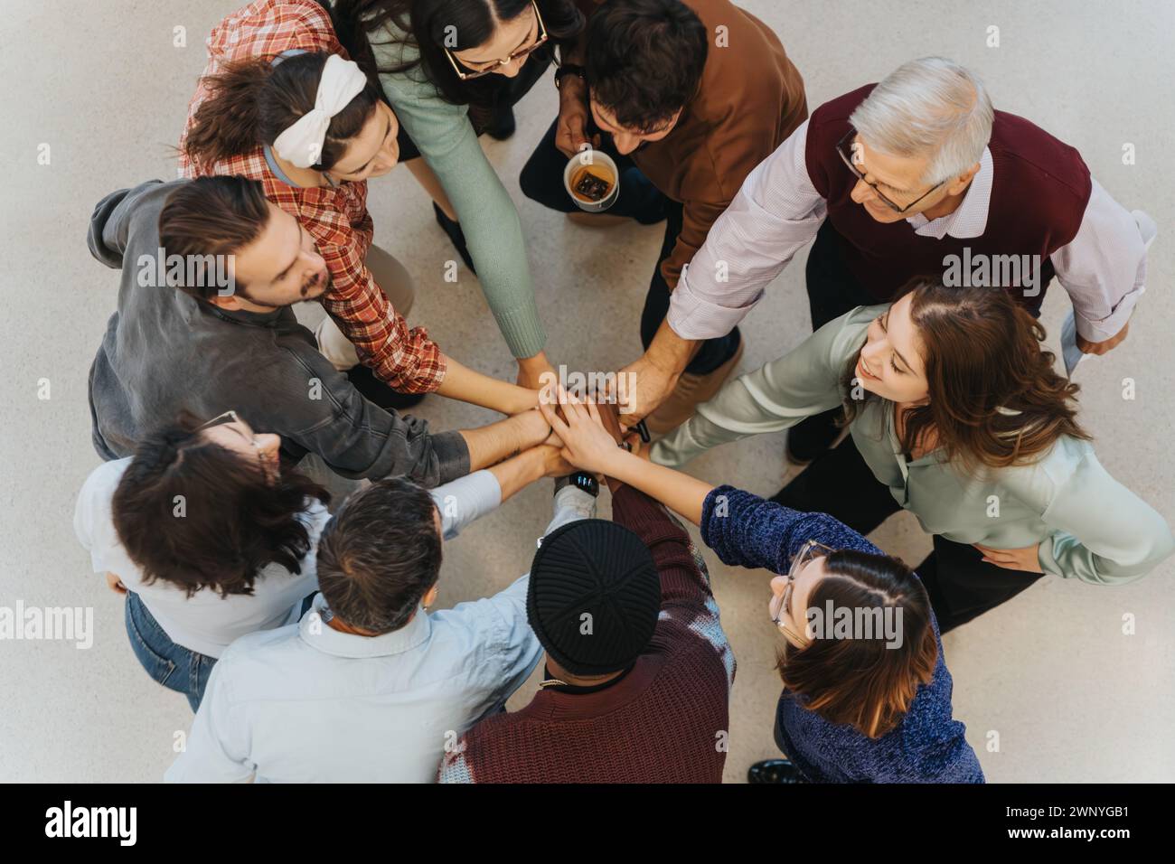 Overhead view of a diverse group of individuals joining hands together in a gesture of unity ...