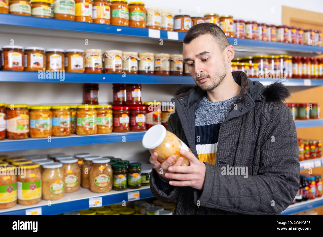 Male shopper selects glass jar of sauerkraut at grocery store. Man ...