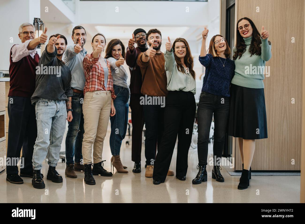 A diverse team of cheerful colleagues celebrates success with thumbs up ...