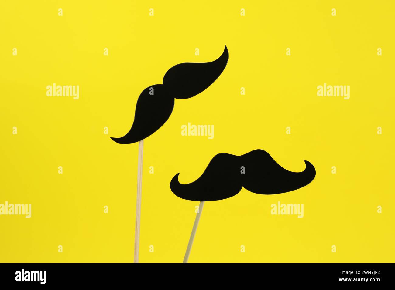 Fake paper mustaches on sticks against yellow background Stock Photo ...