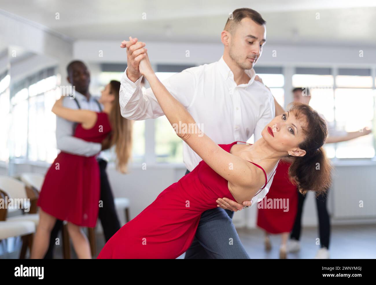 Smiling young woman in elegant red clothes learn to dance couples latin ...